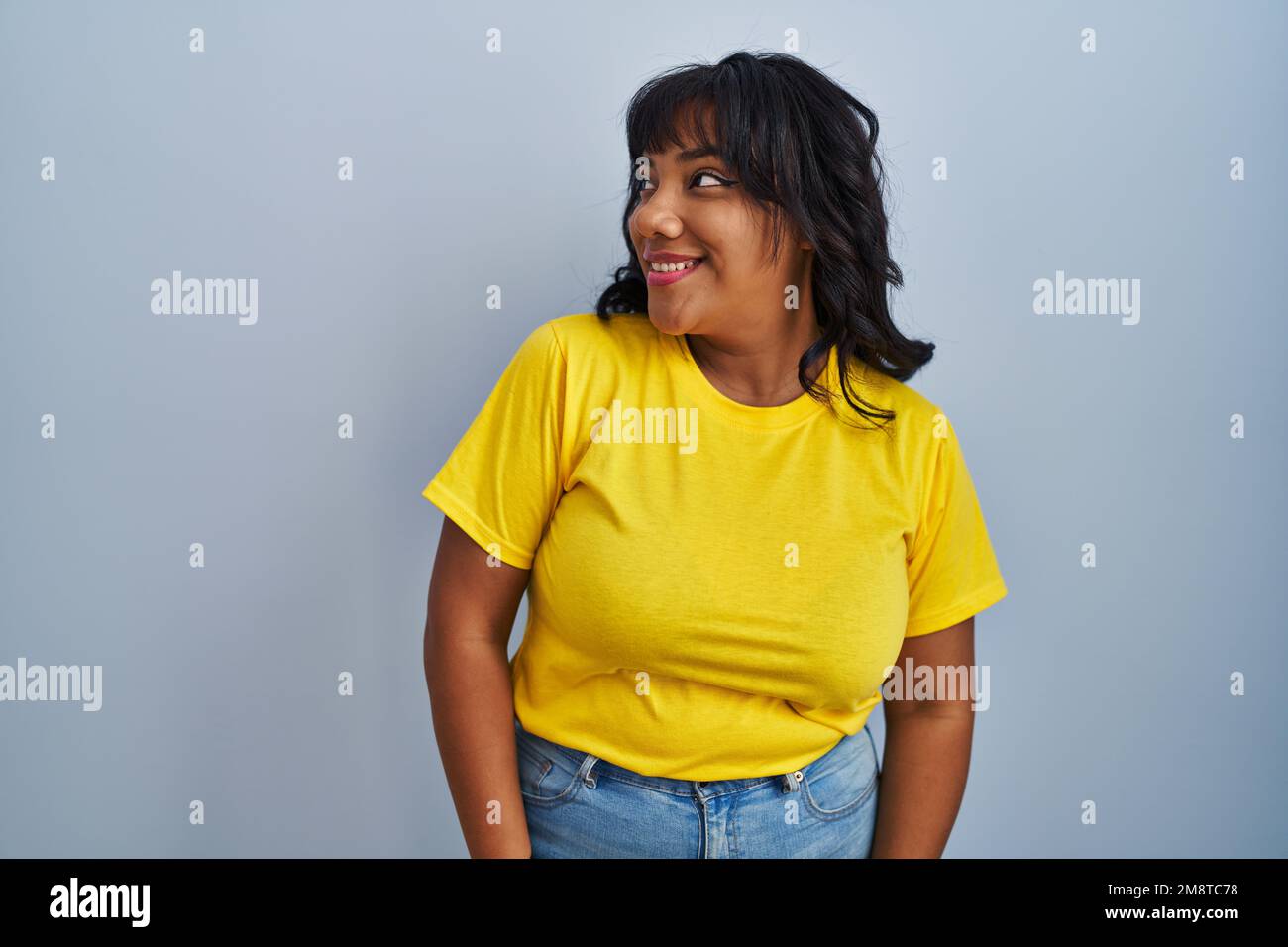 Hispanic woman standing over blue background looking away to side with ...