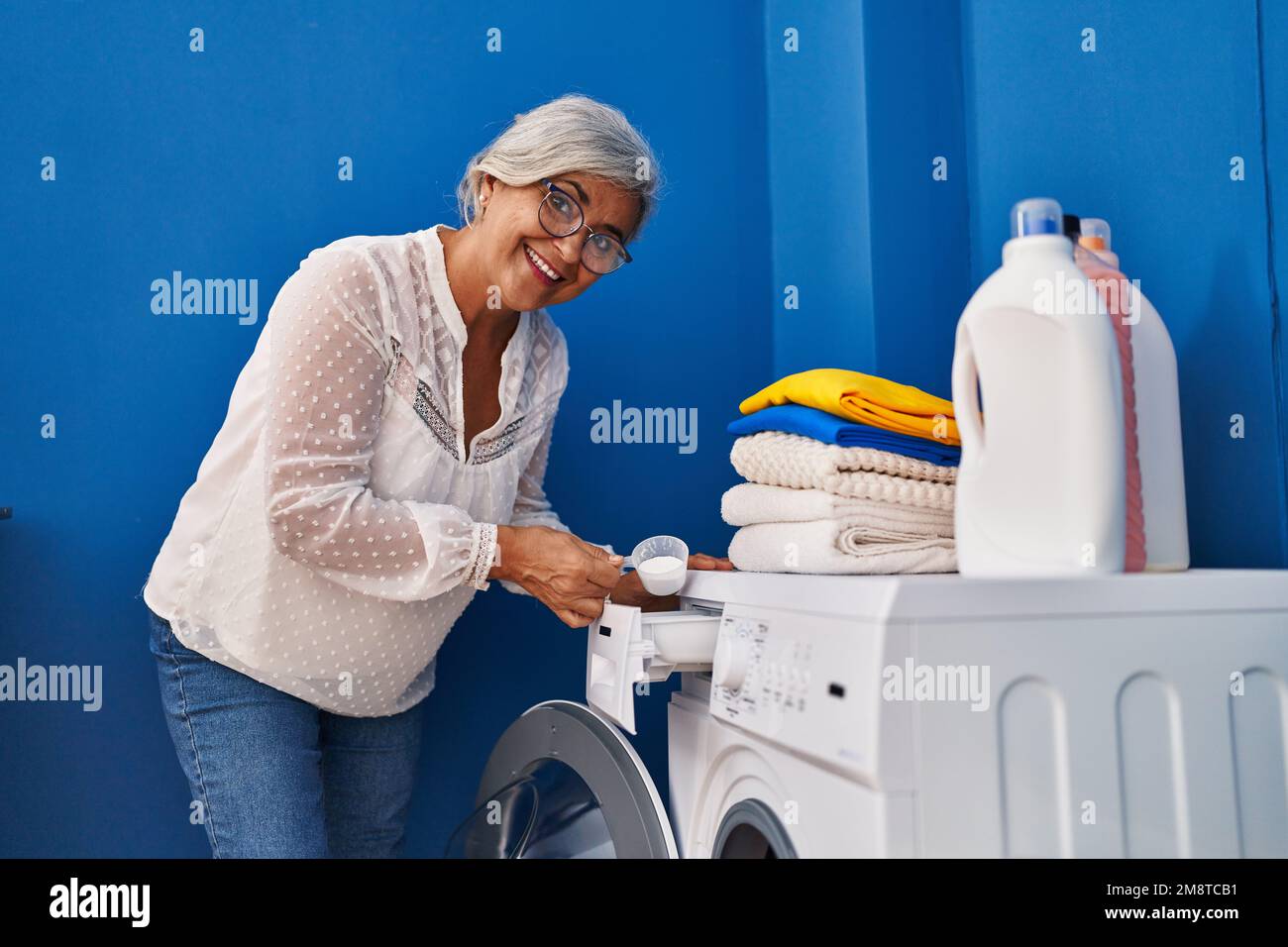 Middle age woman pouring detergent on washing machine at laundry room ...