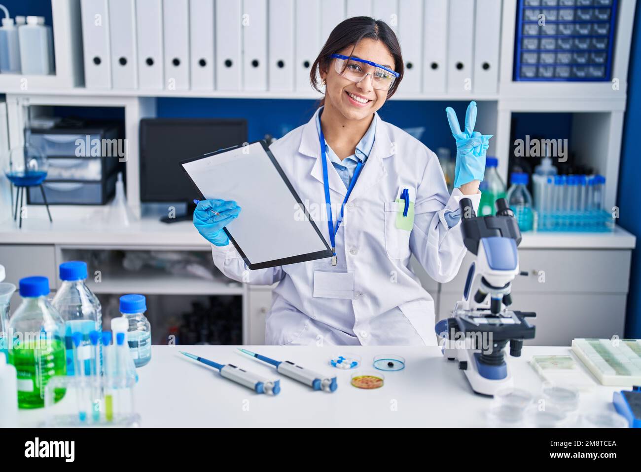 Hispanic young woman working at scientist laboratory smiling looking to ...