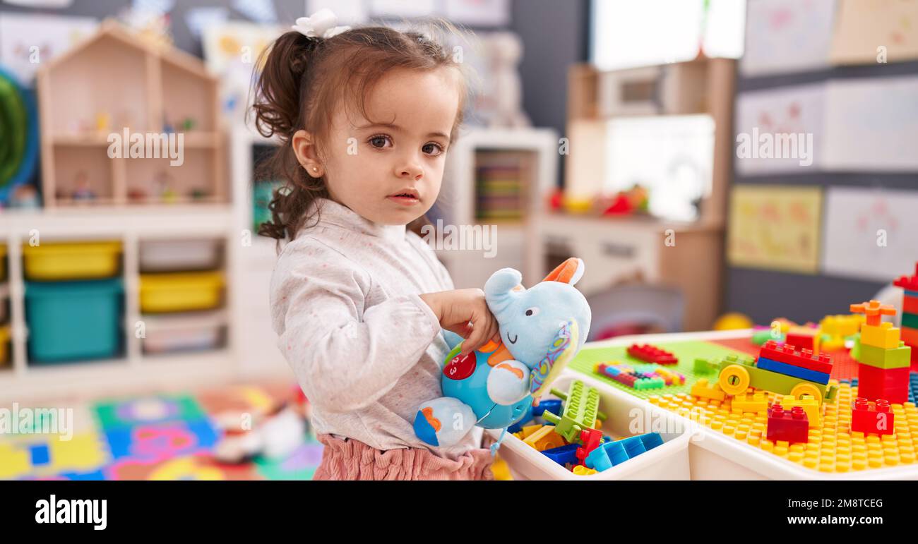 Adorable hispanic toddler holding elephant toy standing at kindergarten ...