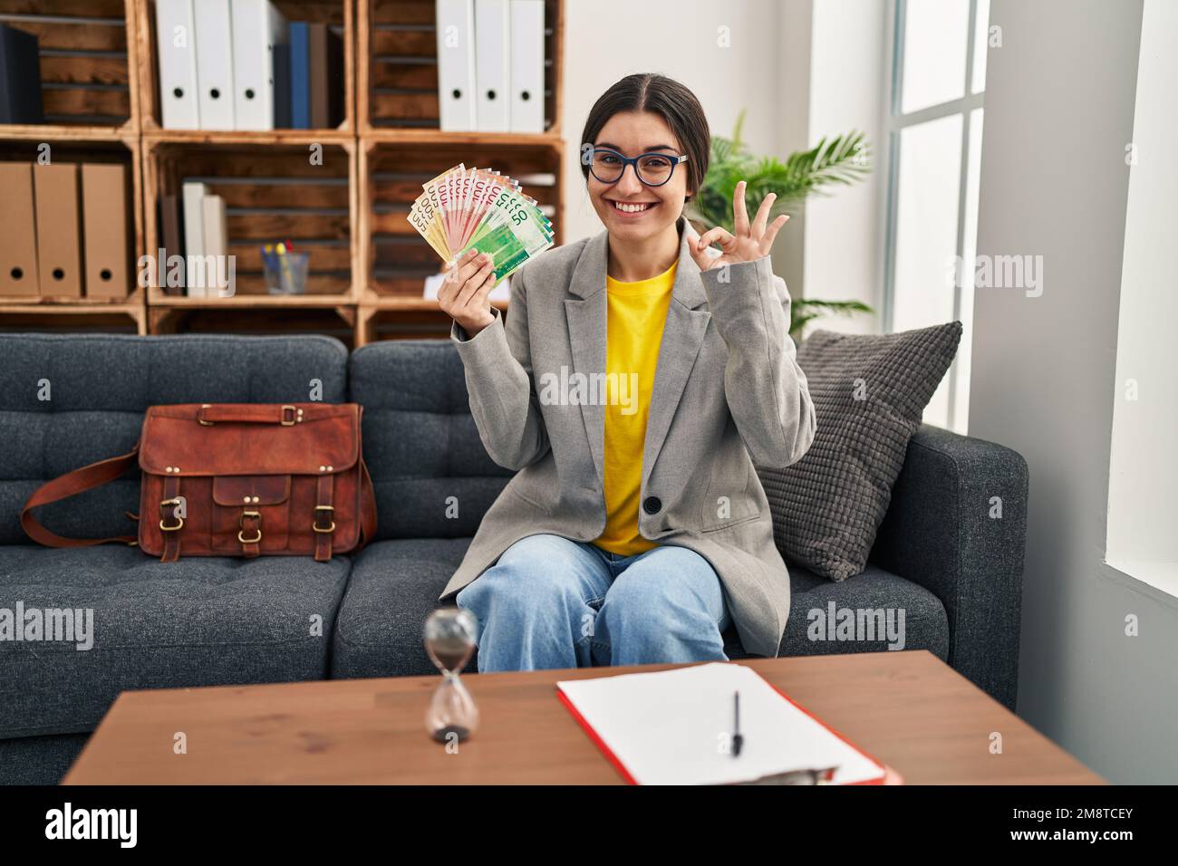 Young hispanic woman working at consultation office holding money doing ...