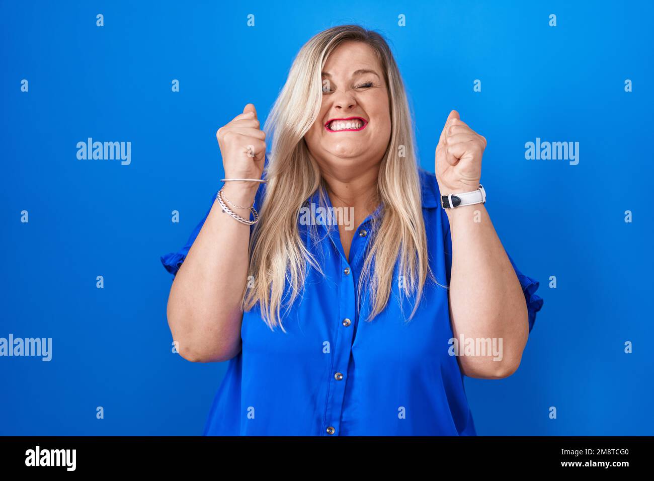 Caucasian plus size woman standing over blue background excited for ...