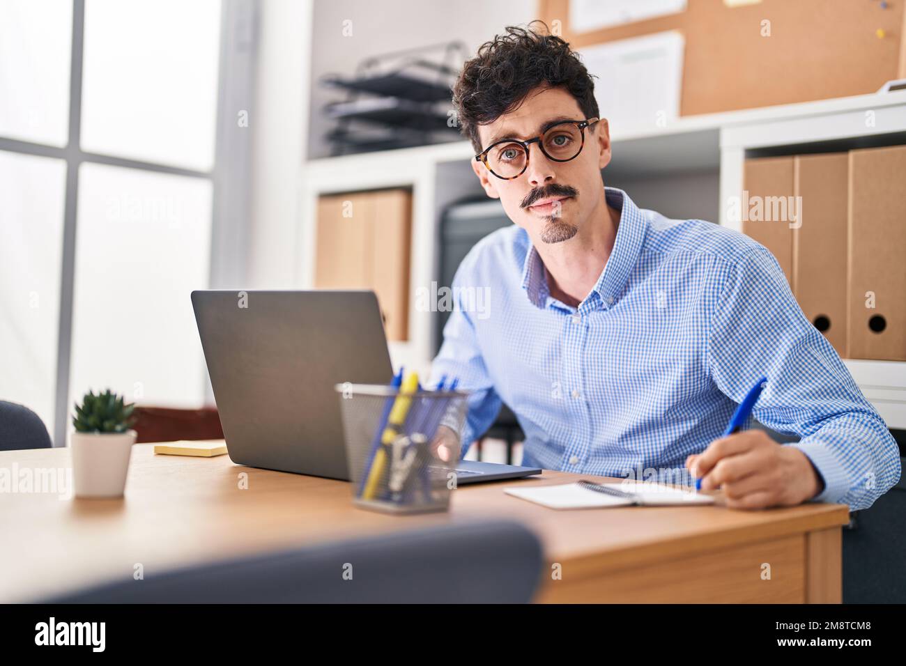 Young caucasian man business worker using laptop writing on notebook at ...