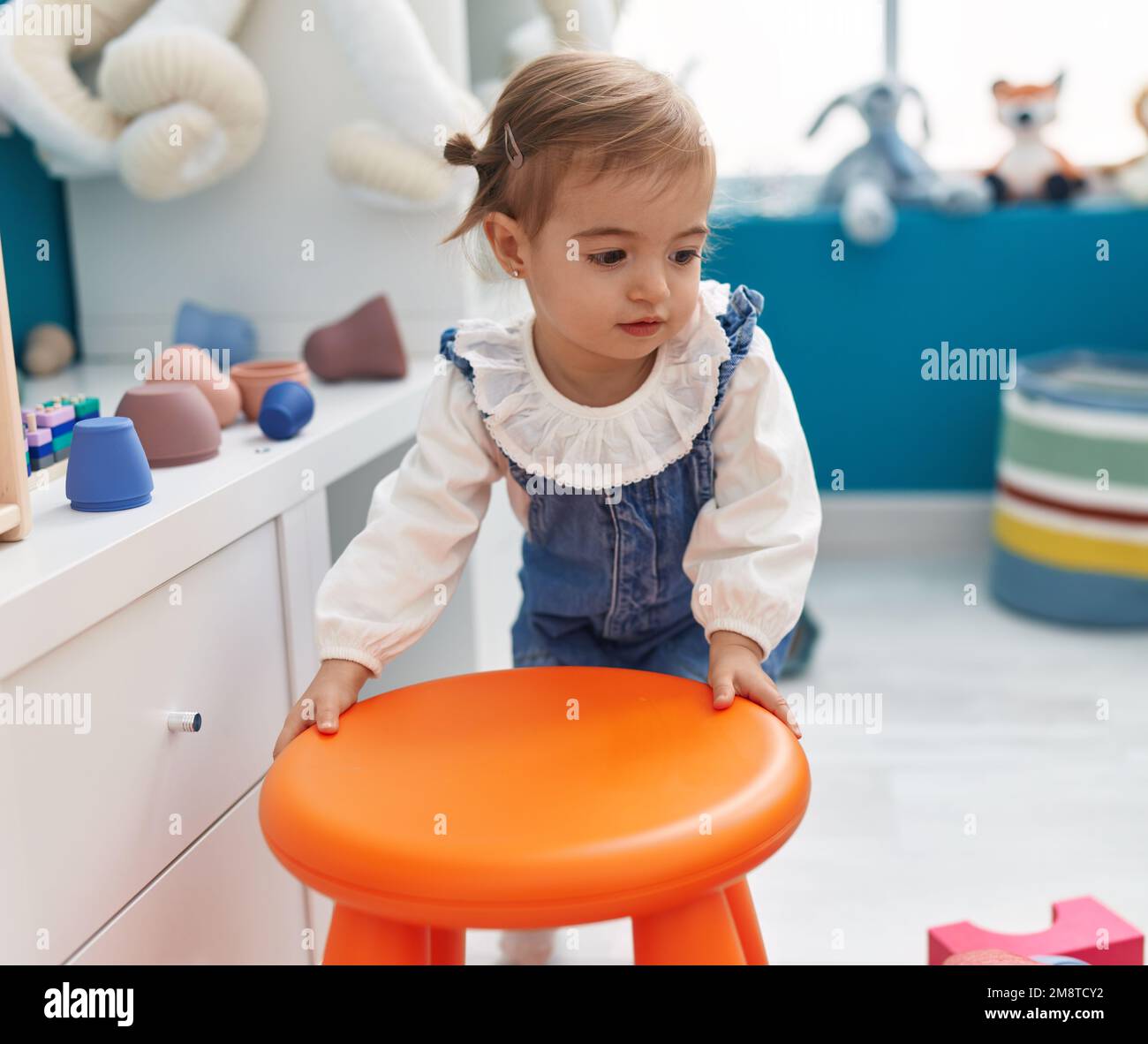 Adorable blonde toddler smiling confident holding chair at kindergarten Stock Photo - Alamy