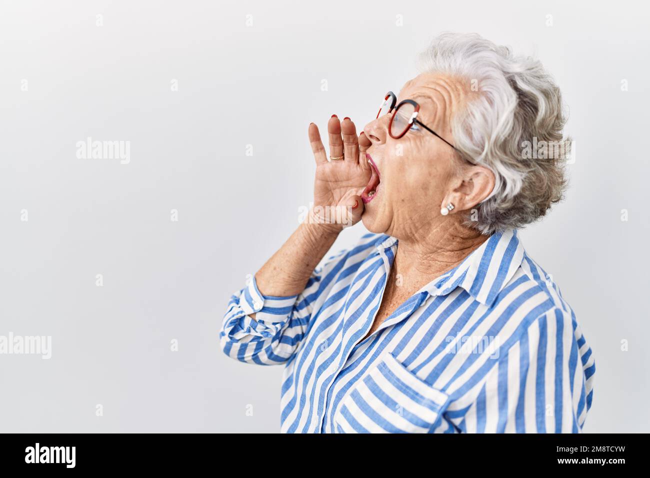 Senior woman with grey hair standing over white background shouting and ...
