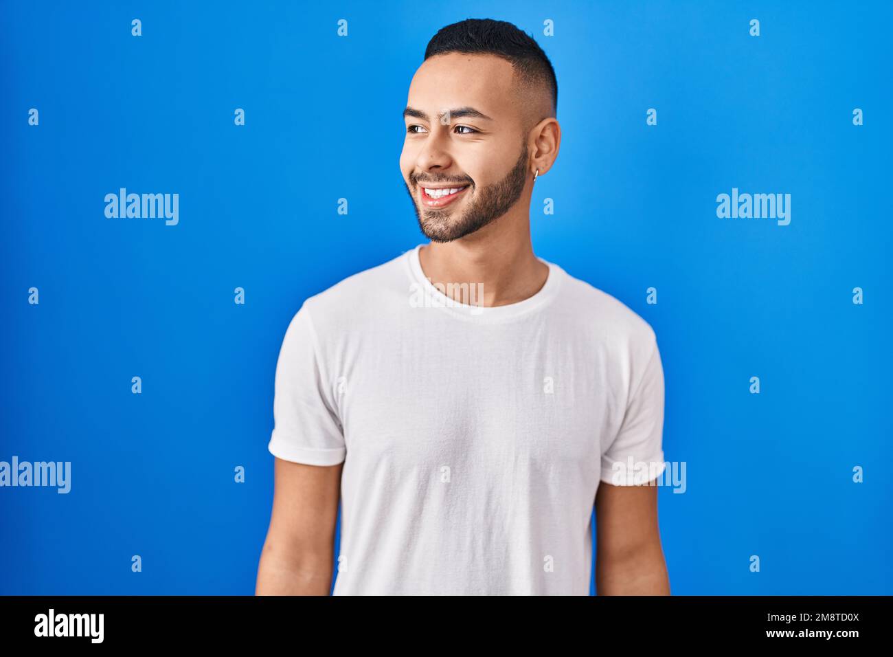 Young hispanic man standing over blue background looking away to side ...