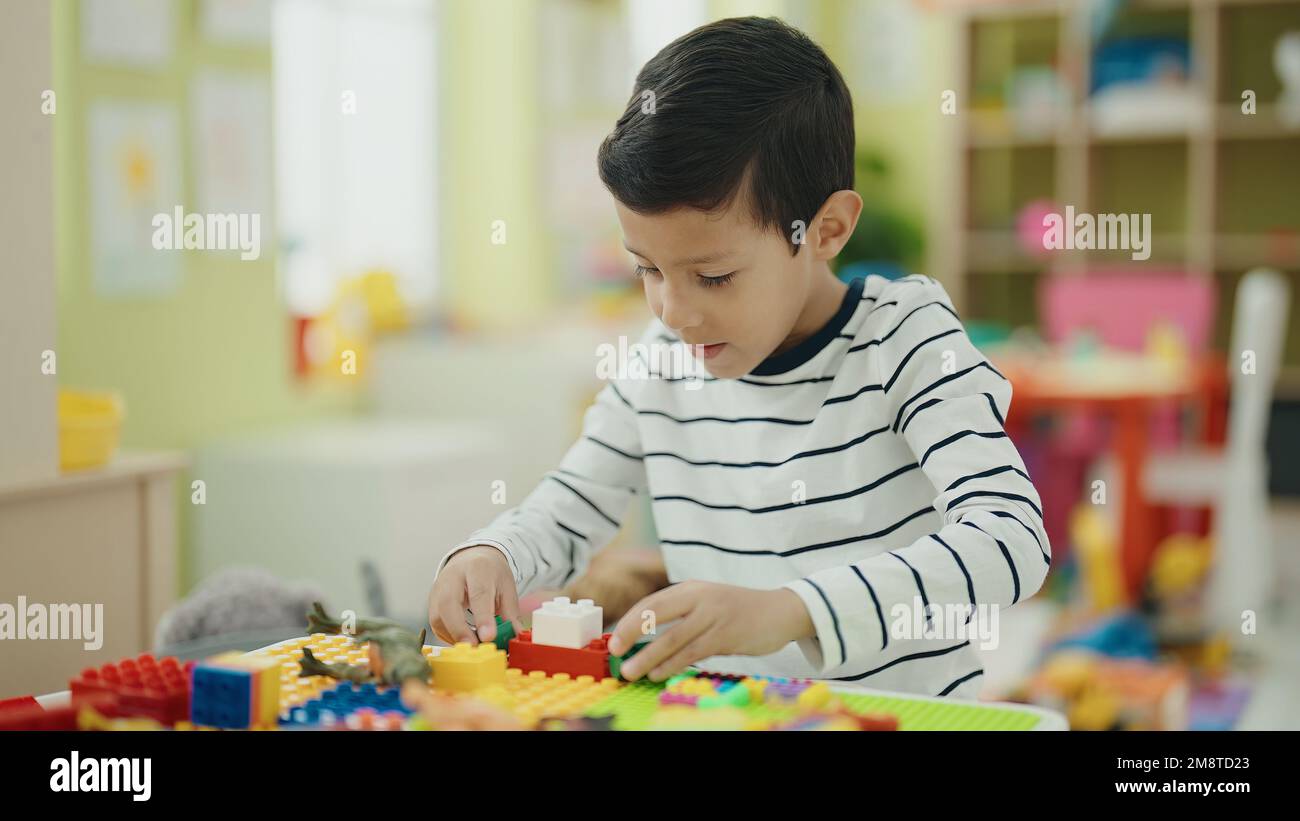 Adorable hispanic boy playing with construction blocks sitting on table ...