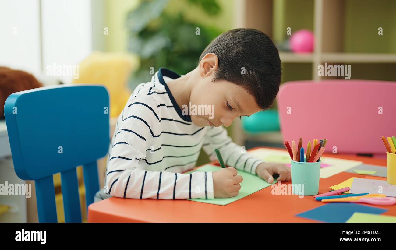 Adorable hispanic boy preschool student sitting on table drawing on ...