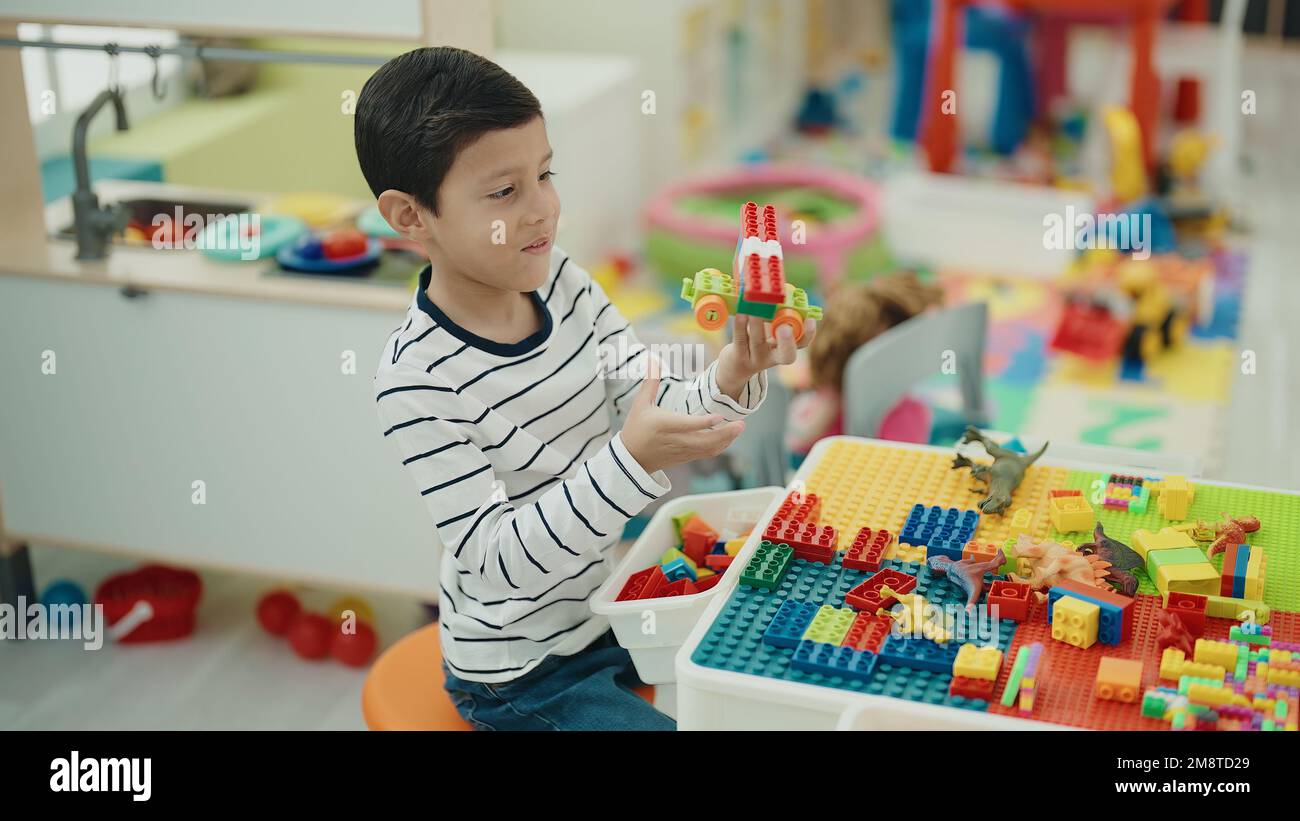 Adorable hispanic boy playing with construction blocks sitting on table ...