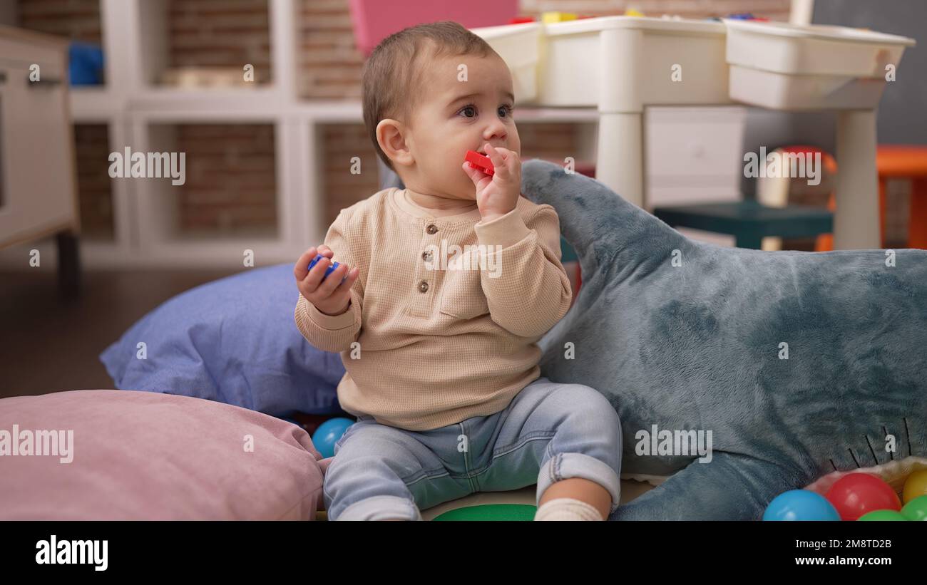 Adorable toddler bitting plastic construction blocks sitting on floor ...