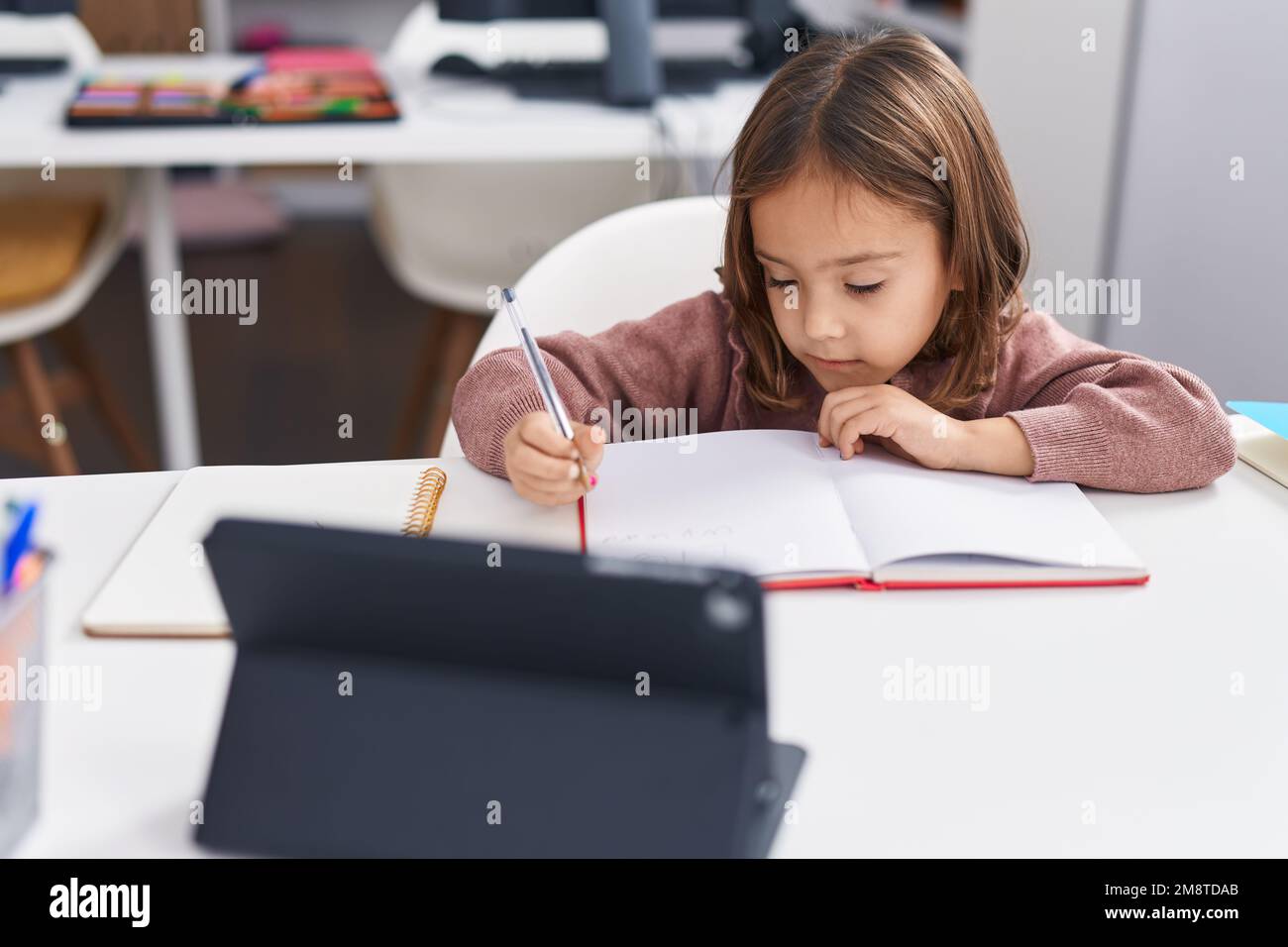 Adorable hispanic girl student sitting on table studying at classroom ...