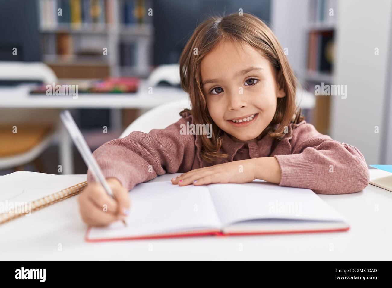 Adorable hispanic girl student sitting on table doing homework at ...