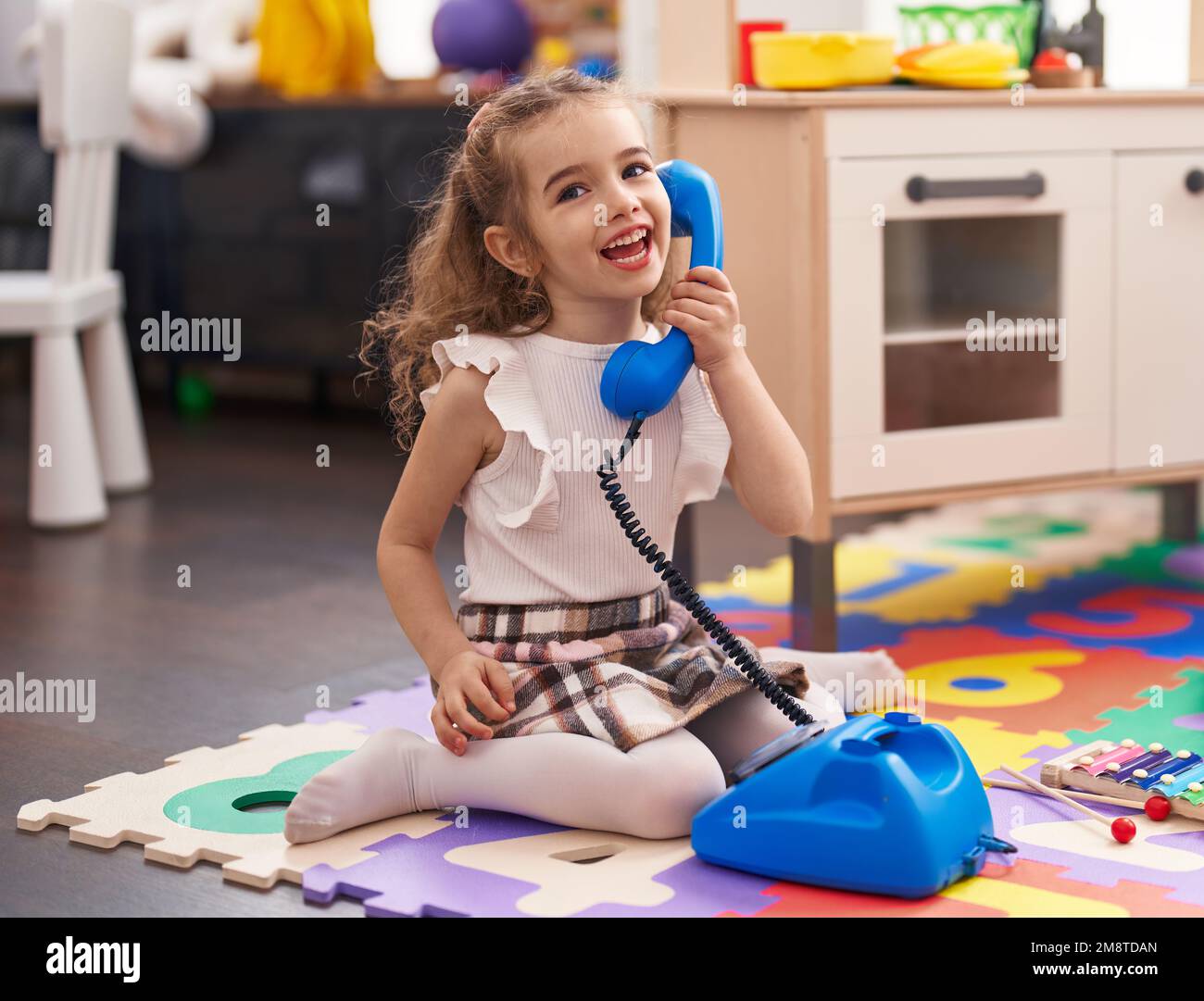 Adorable caucasian girl playing with telephone toy sitting on floor at ...