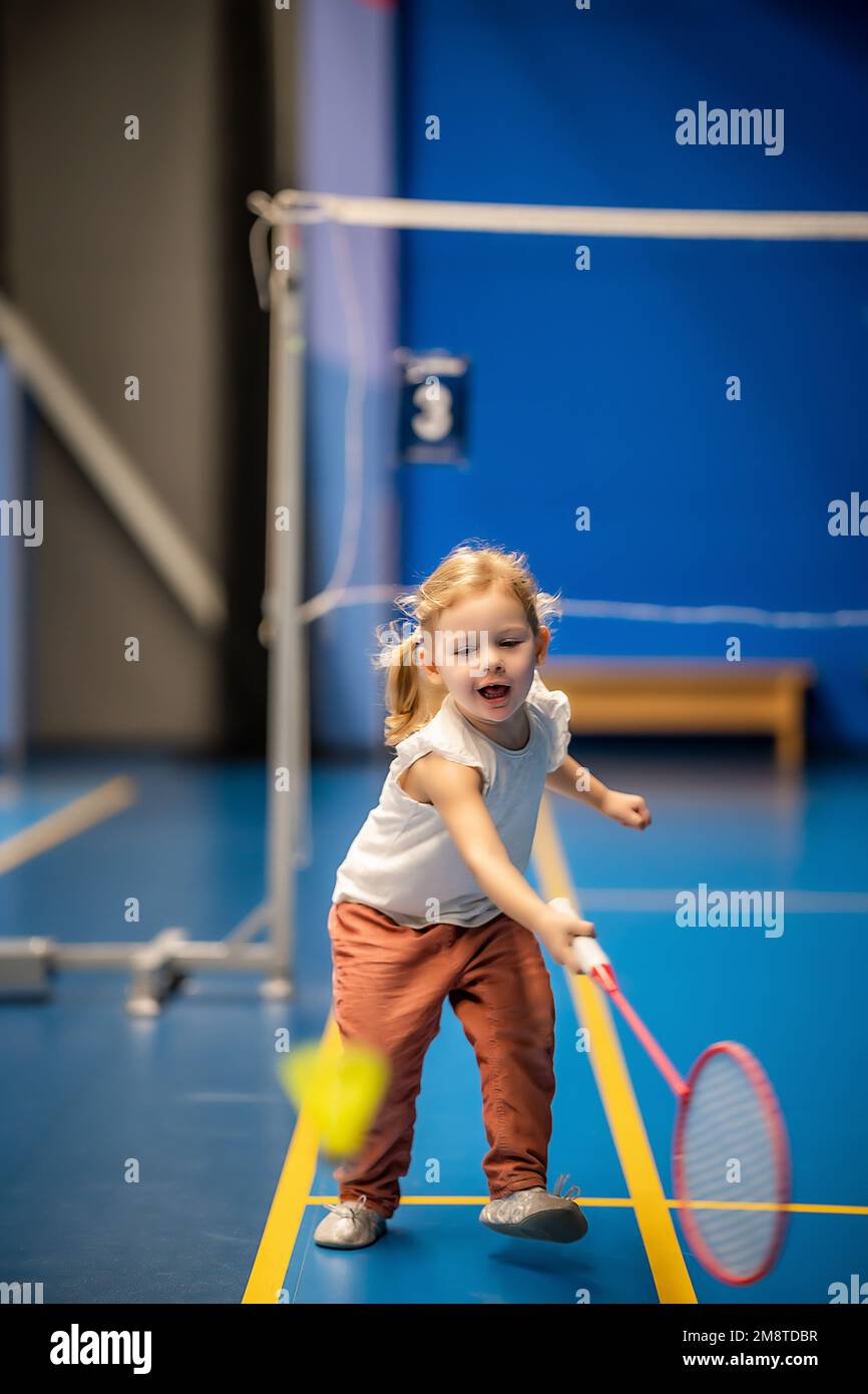 Little girl three years old playing badminton in sport wear on indoor ...