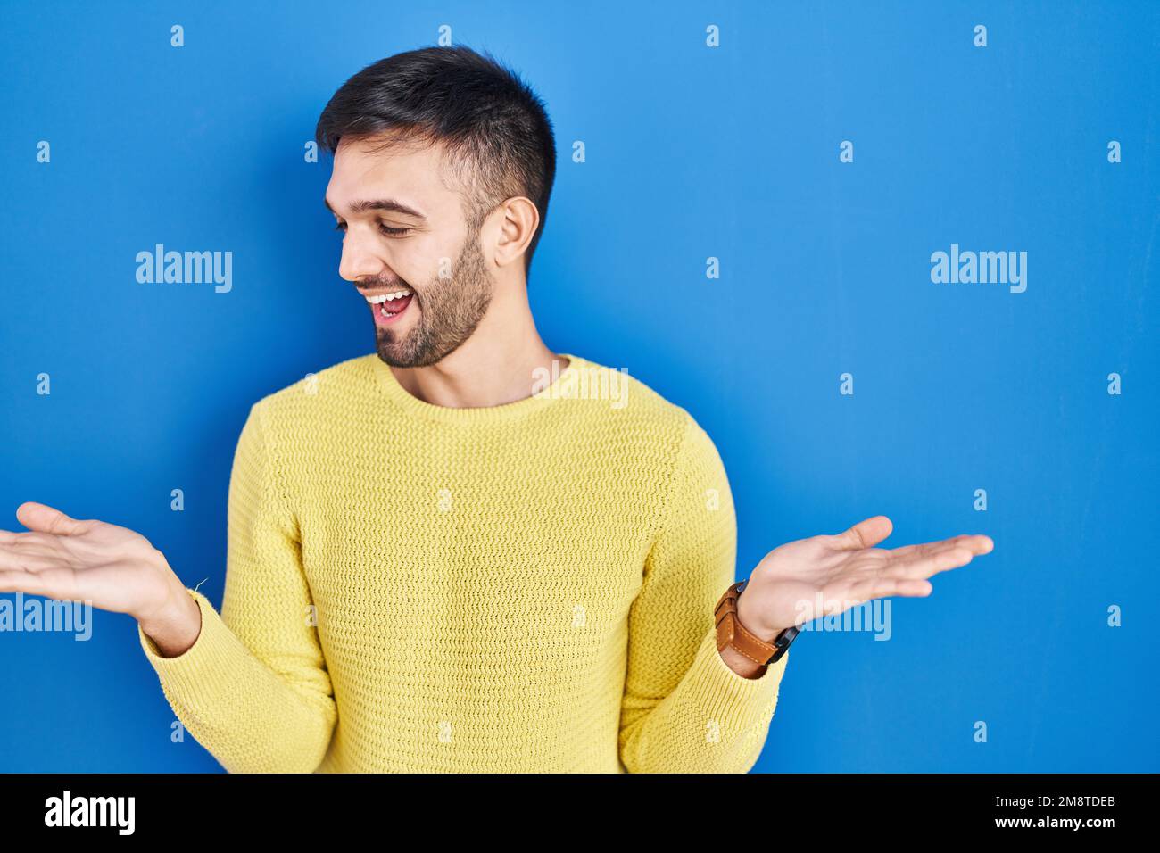 Hispanic man standing over blue background smiling showing both hands ...