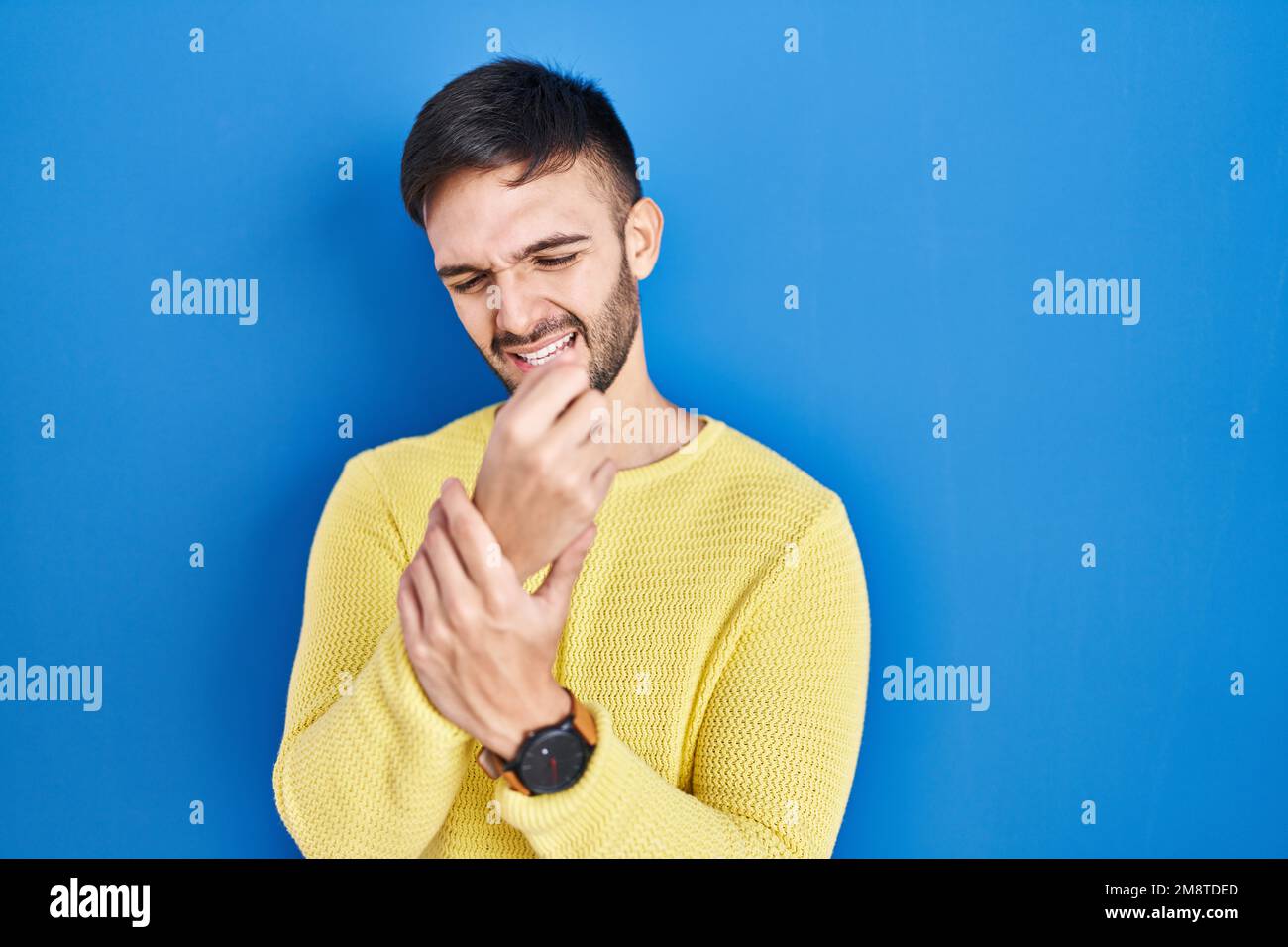 Hispanic man standing over blue background suffering pain on hands and ...