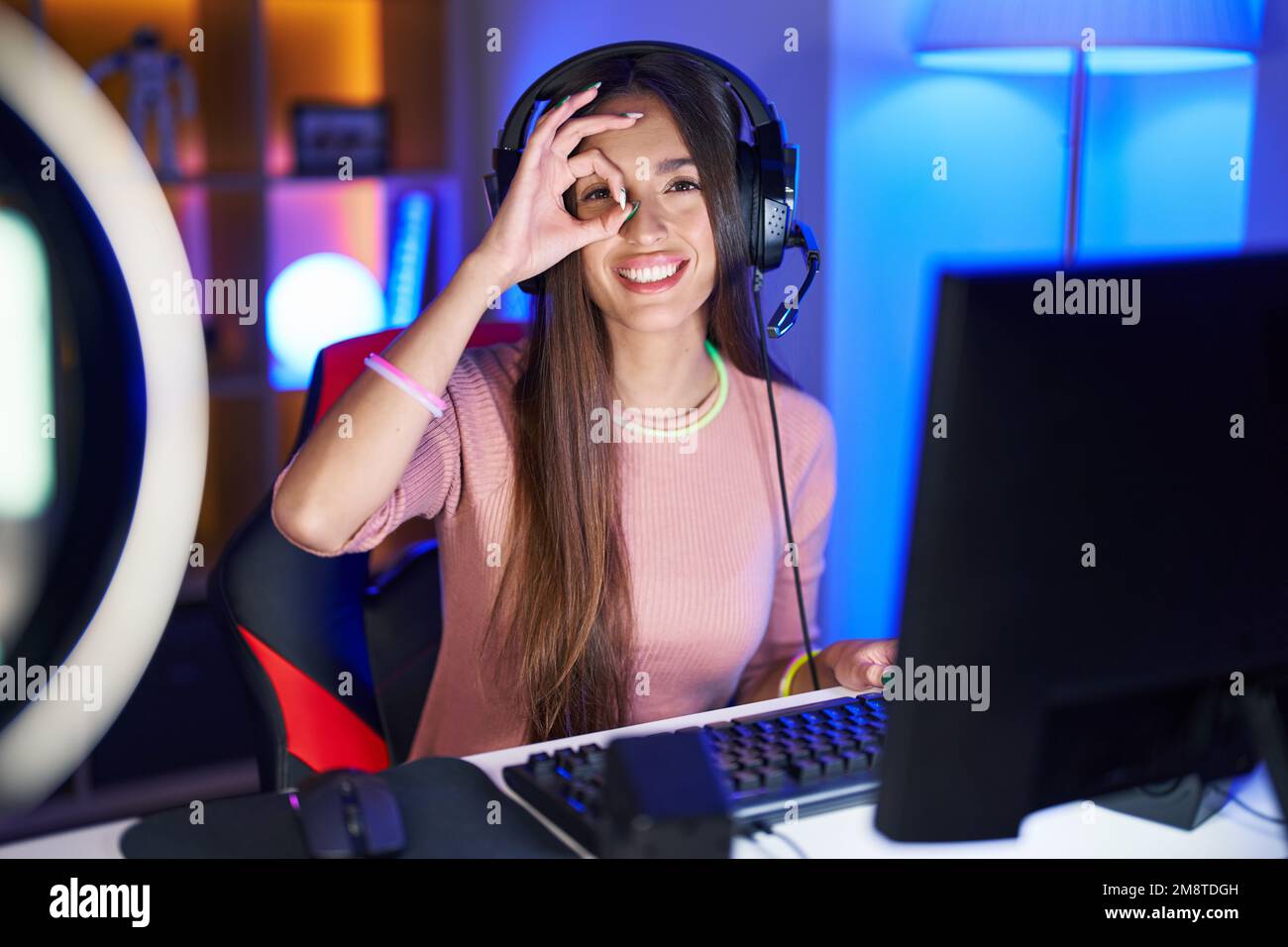 Young hispanic woman playing video games doing ok gesture with hand ...