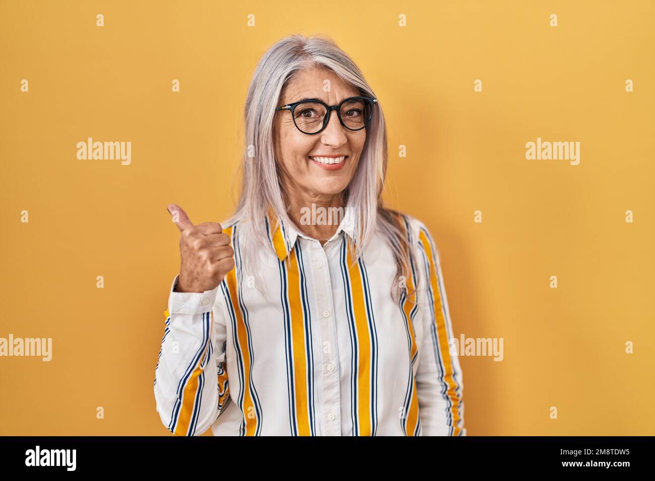 Middle age woman with grey hair standing over yellow background wearing ...