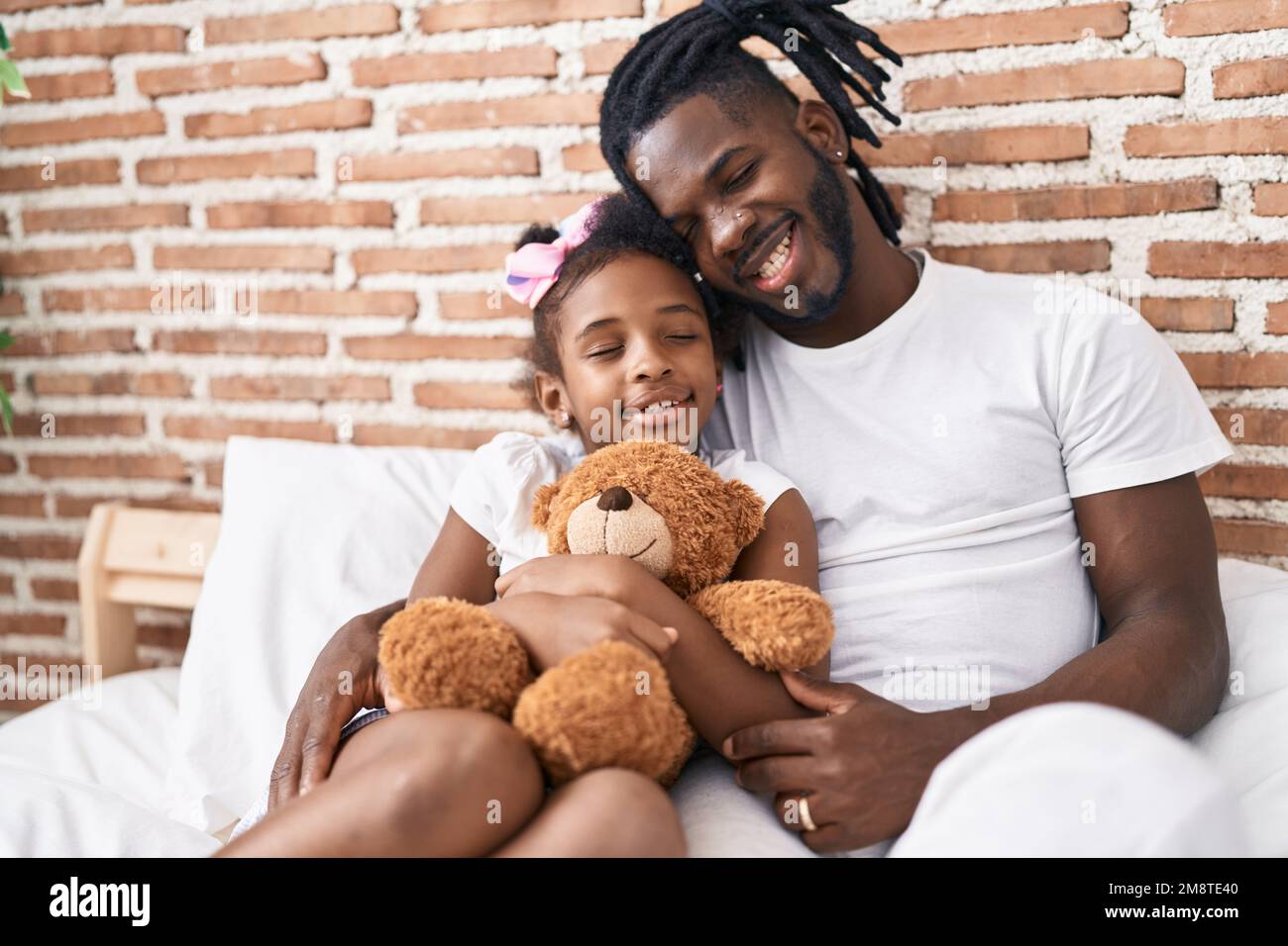 Father and daughter hugging each other sitting on bed holding teddy ...