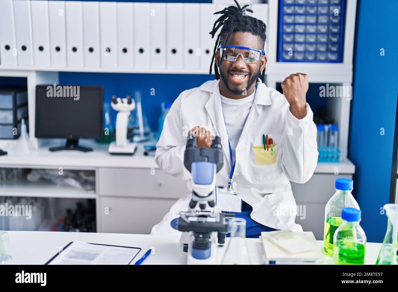 African man with dreadlocks working at scientist laboratory celebrating surprised and amazed for ...