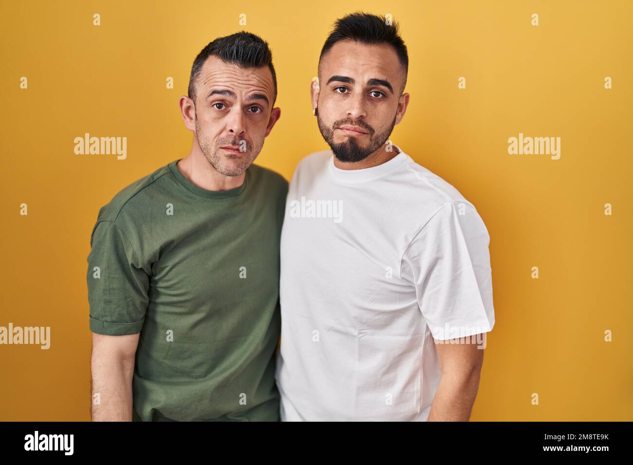 Homosexual couple standing over yellow background depressed and worry ...