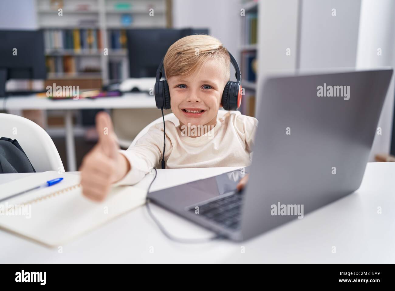Adorable toddler student using laptop doing ok gesture with thumb up at ...
