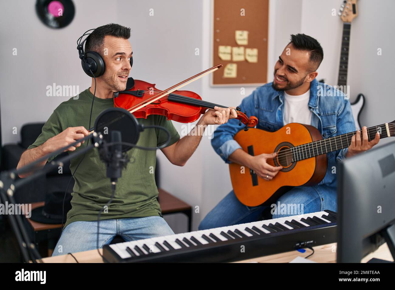 Two men musicians playing classical guitar and violin at music studio ...