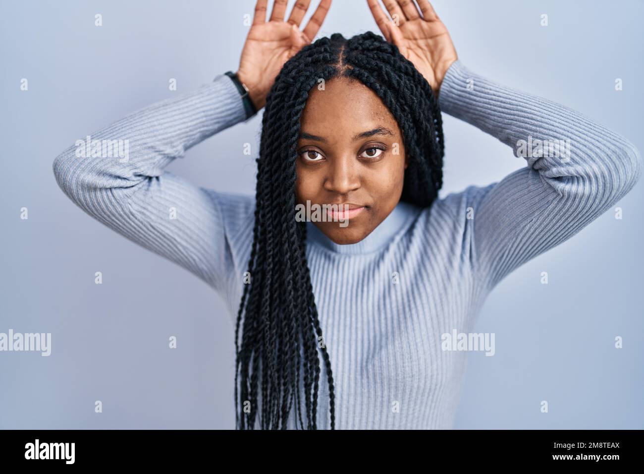 African american woman standing over blue background doing bunny ears ...