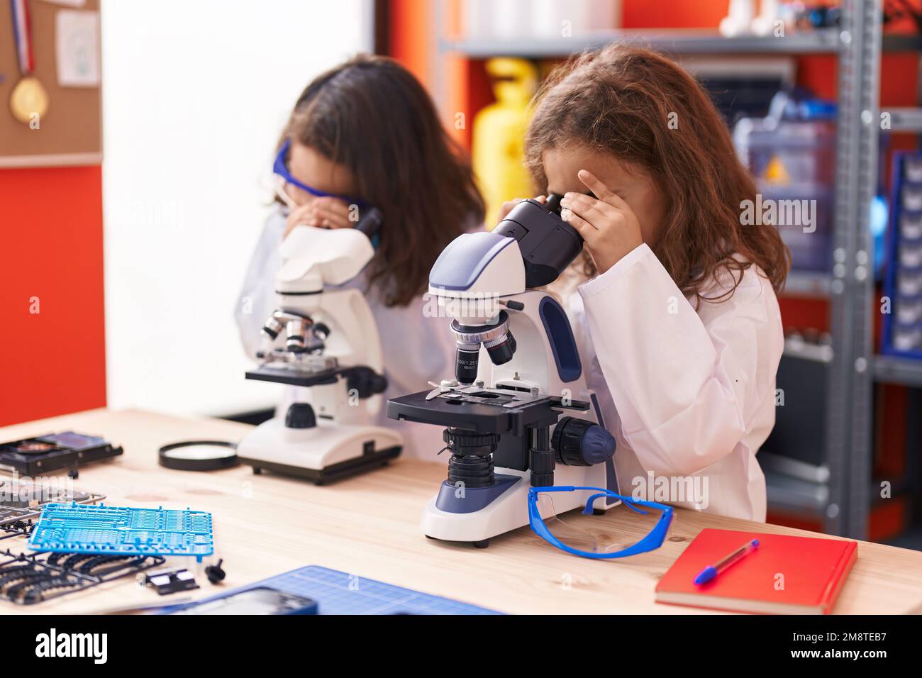 Two kids students using microscopes standing at laboratory classroom ...