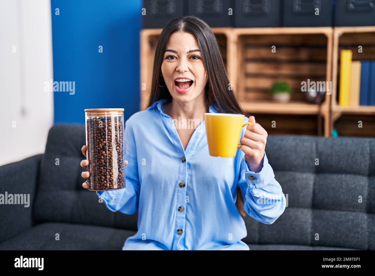 Young brunette woman holding coffee beans and cup of coffee celebrating ...