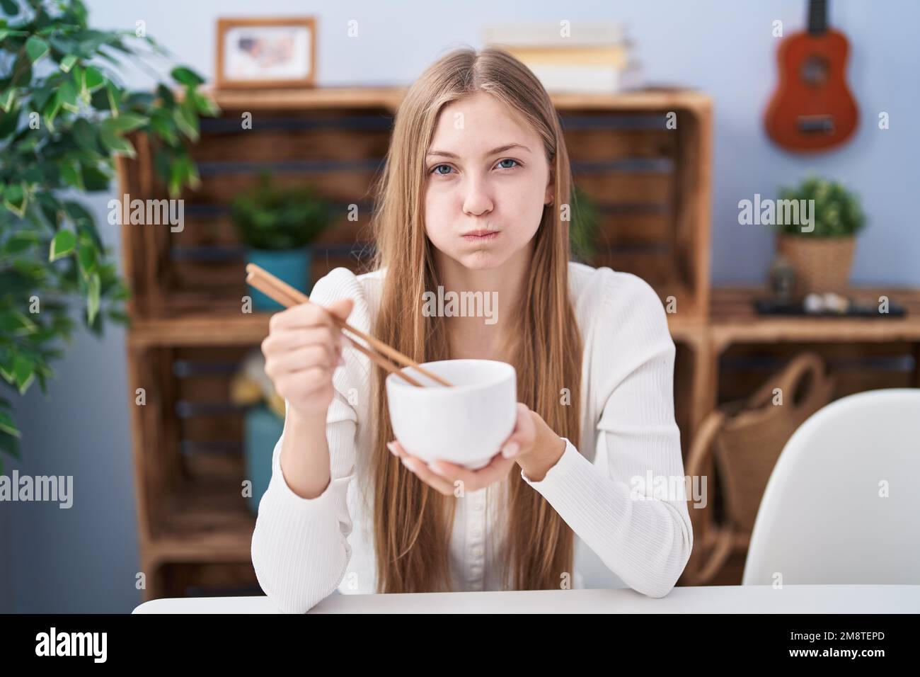 Young caucasian woman eating asian food using chopsticks puffing cheeks ...