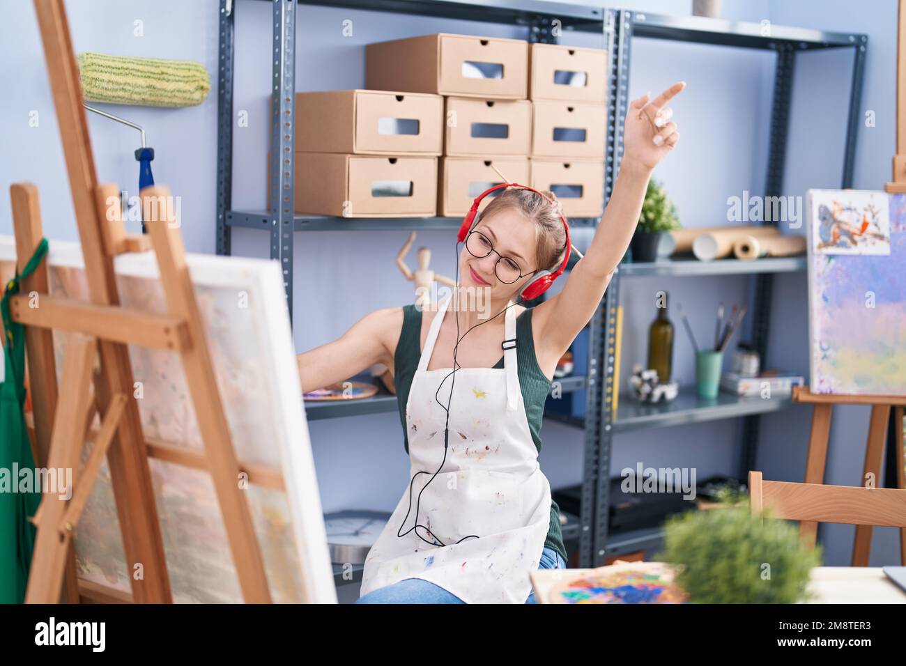 Young caucasian woman artist listening to music drawing at art studio ...