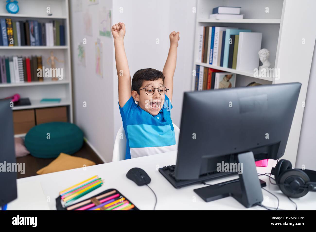Adorable hispanic boy student using laptop with cheerful expression at ...