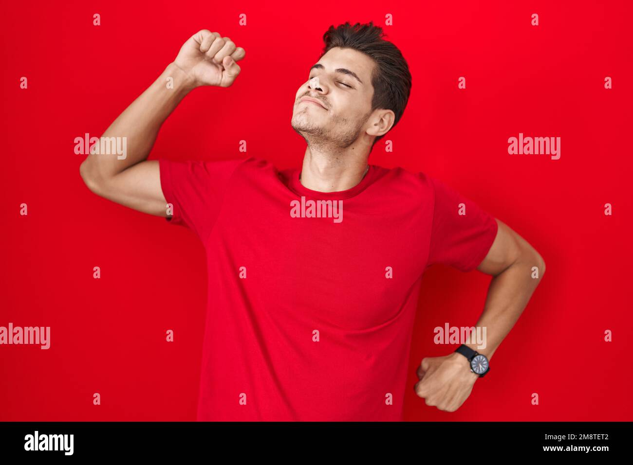 Young hispanic man standing over red background stretching back, tired ...