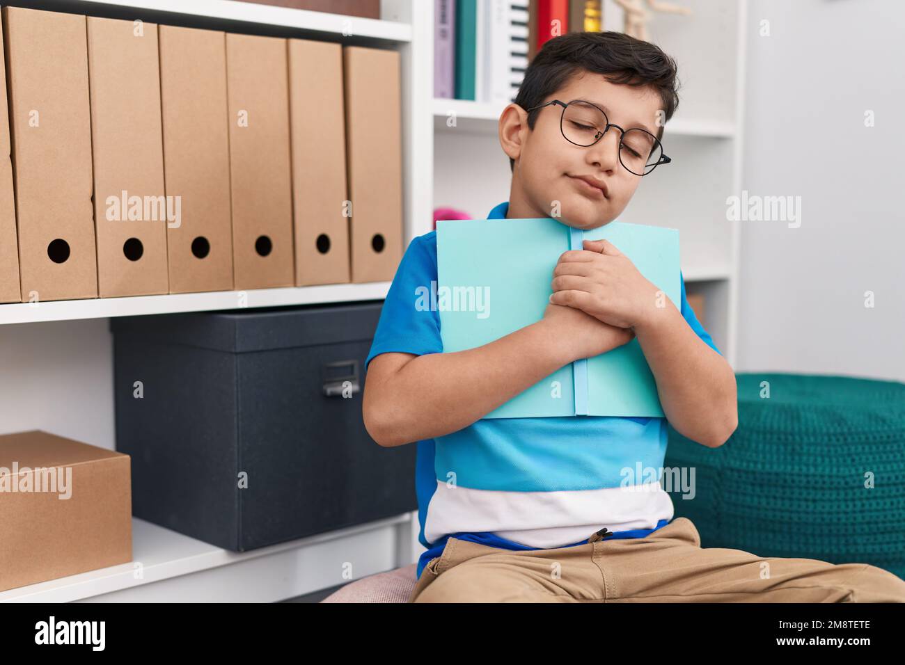 Adorable hispanic boy student hugging book at library school Stock ...