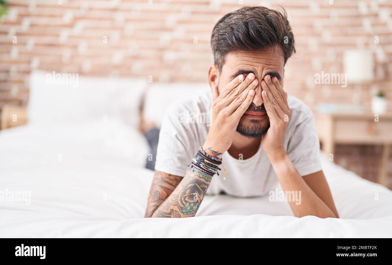 Young hispanic man lying on bed rubbing eyes at bedroom Stock Photo - Alamy