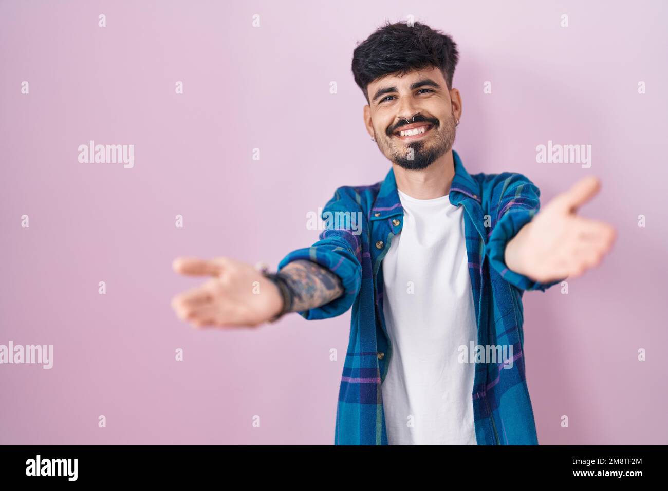 Young hispanic man with beard standing over pink background looking at ...
