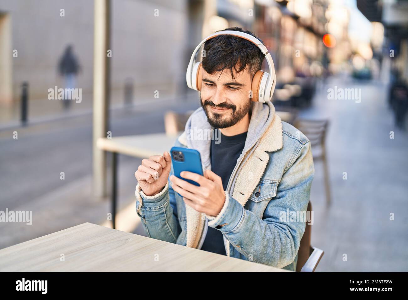Young hispanic man listening to music sitting on table at coffee shop ...