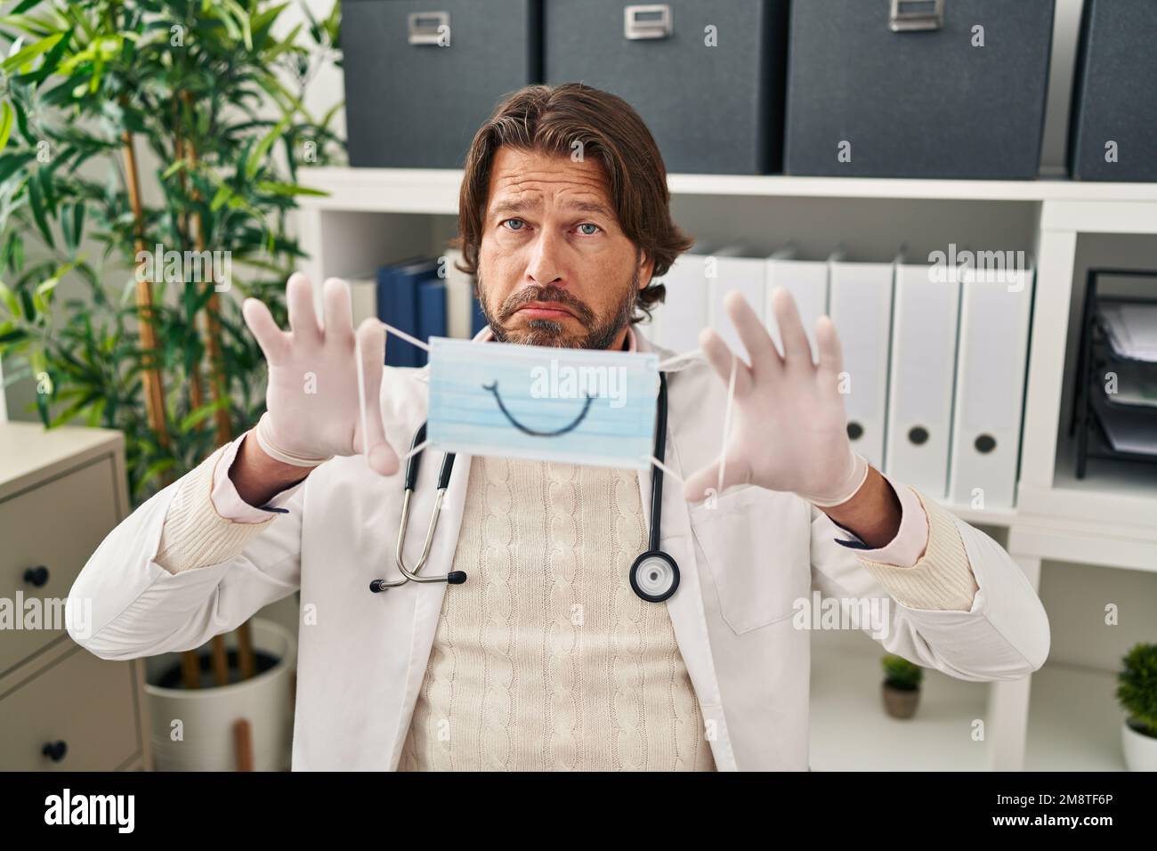 Handsome middle age doctor man wearing safety mask depressed and worry ...