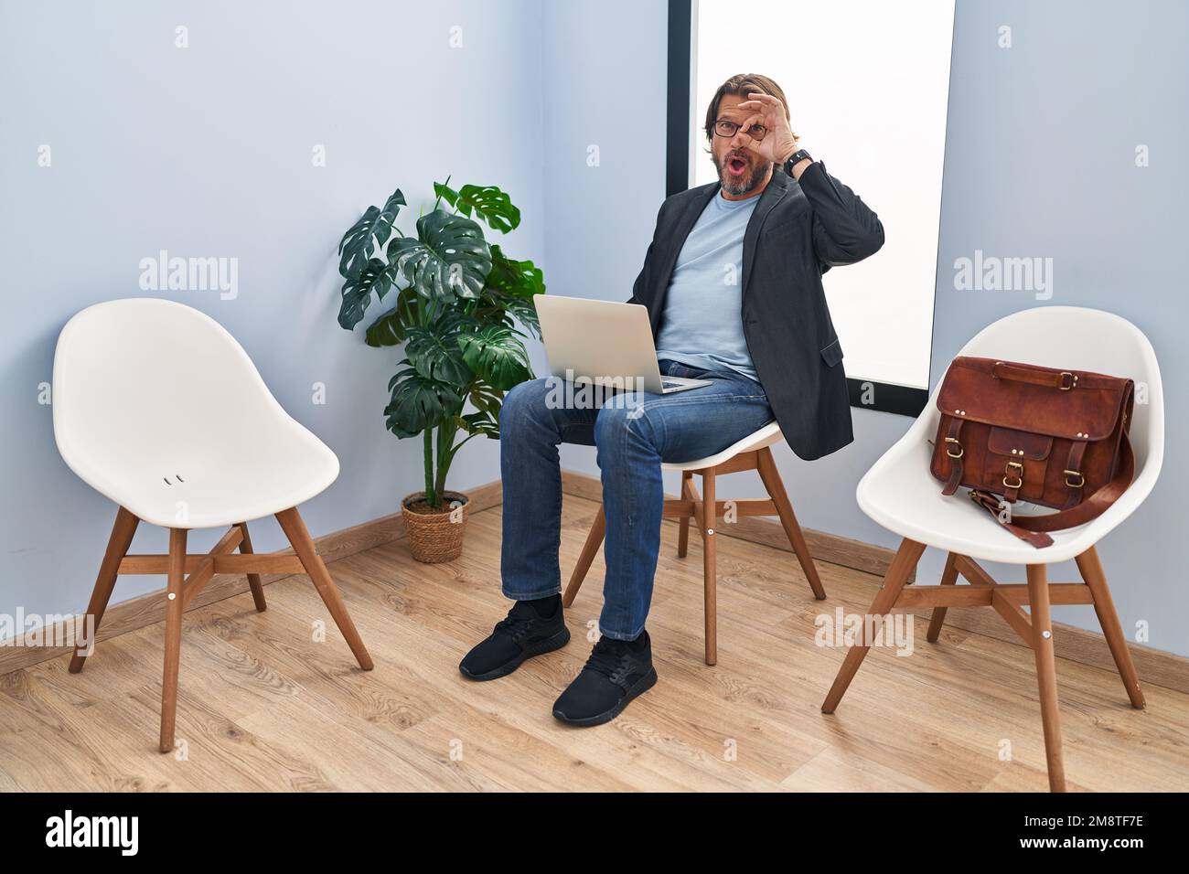 Handsome middle age man sitting at waiting room working with laptop ...