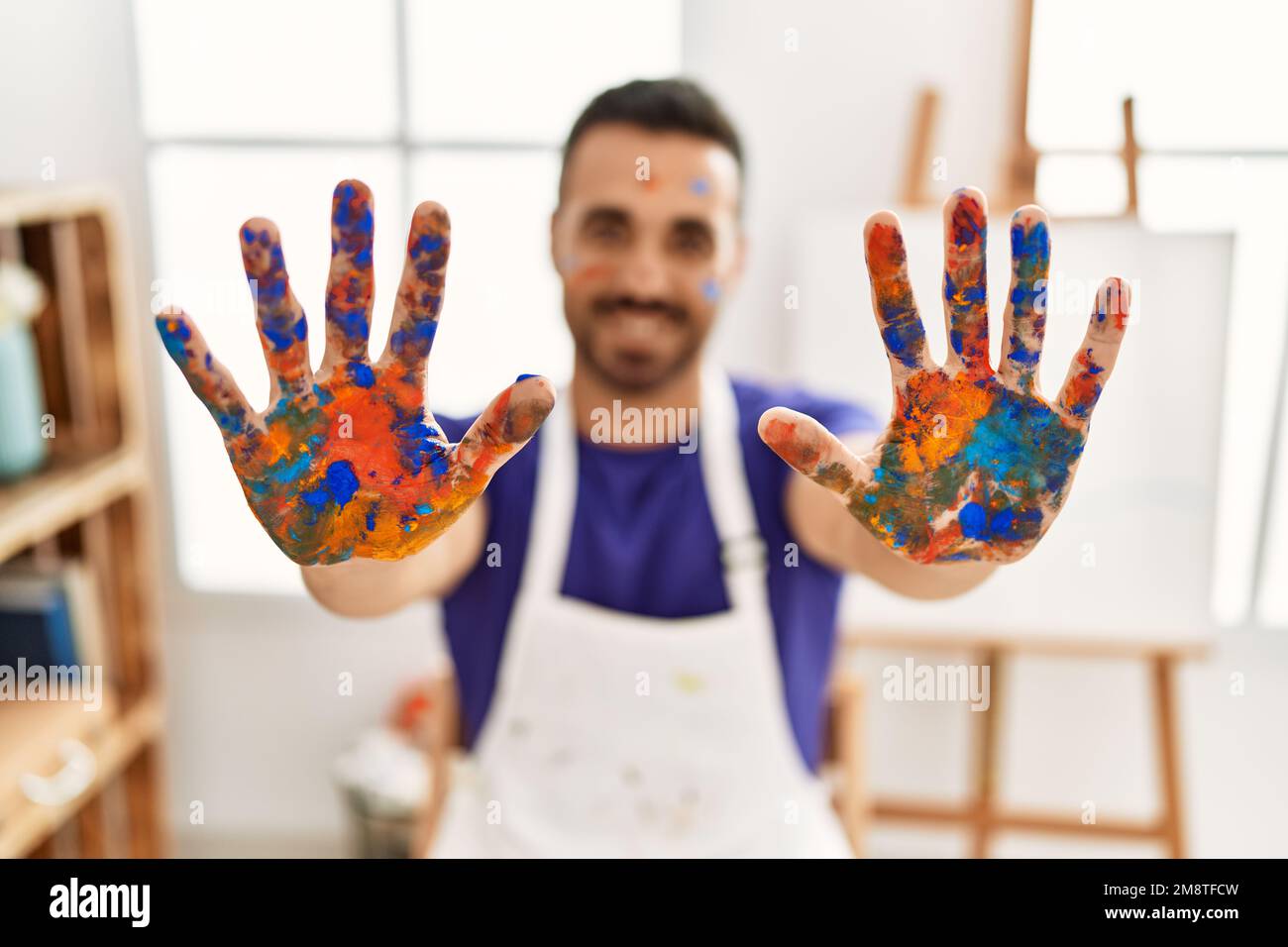 Young hispanic man smiling confident showing painted palm hands at art ...