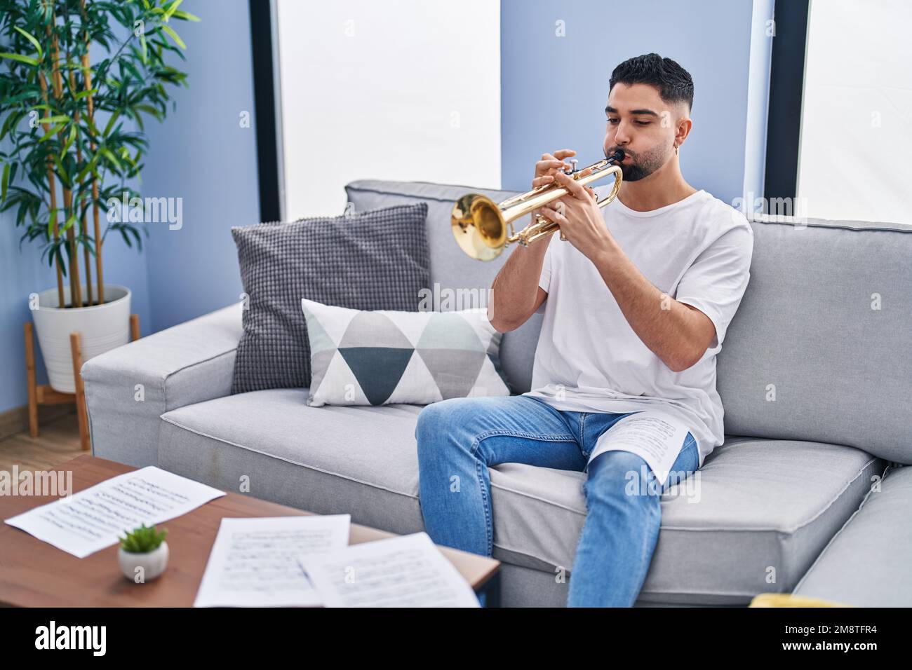 Young arab man musician playing trumpet sitting on sofa at home Stock ...