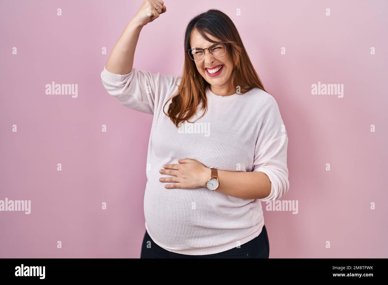Pregnant woman standing over pink background angry and mad raising fist ...