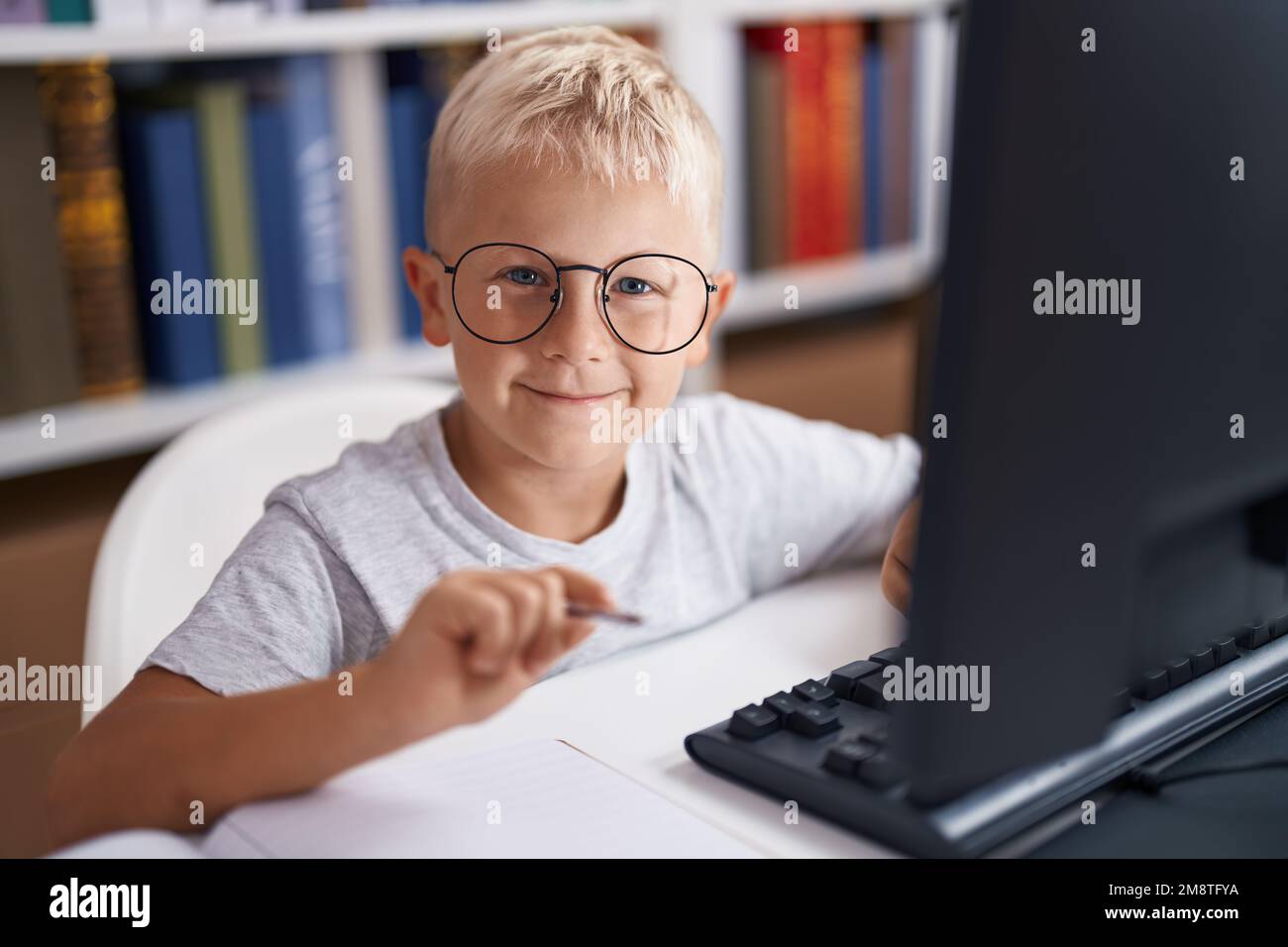 Adorable toddler student using computer sitting on table at classroom ...