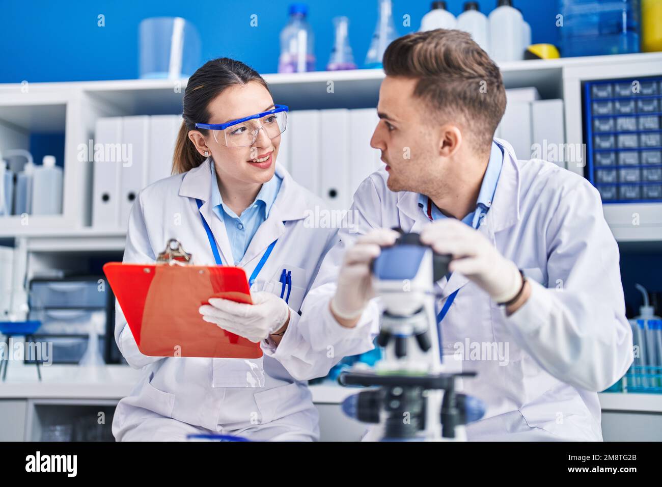 Man and woman scientists using microscope write on clipboard at laboratory Stock Photo - Alamy