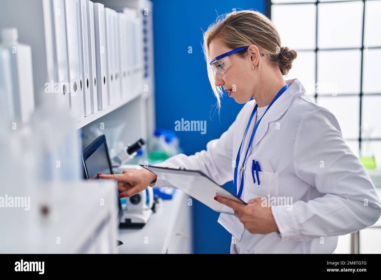 Young blonde woman scientist using computer reading document at ...