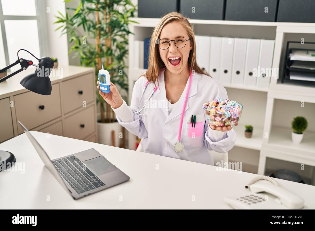Young blonde doctor woman holding glucometer and sweets smiling and ...
