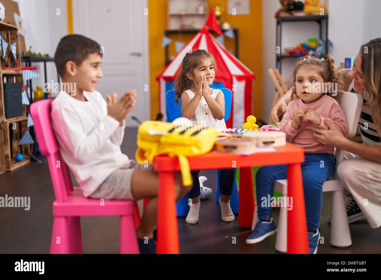 Teacher and group of kids sitting on table applauding at kindergarten ...