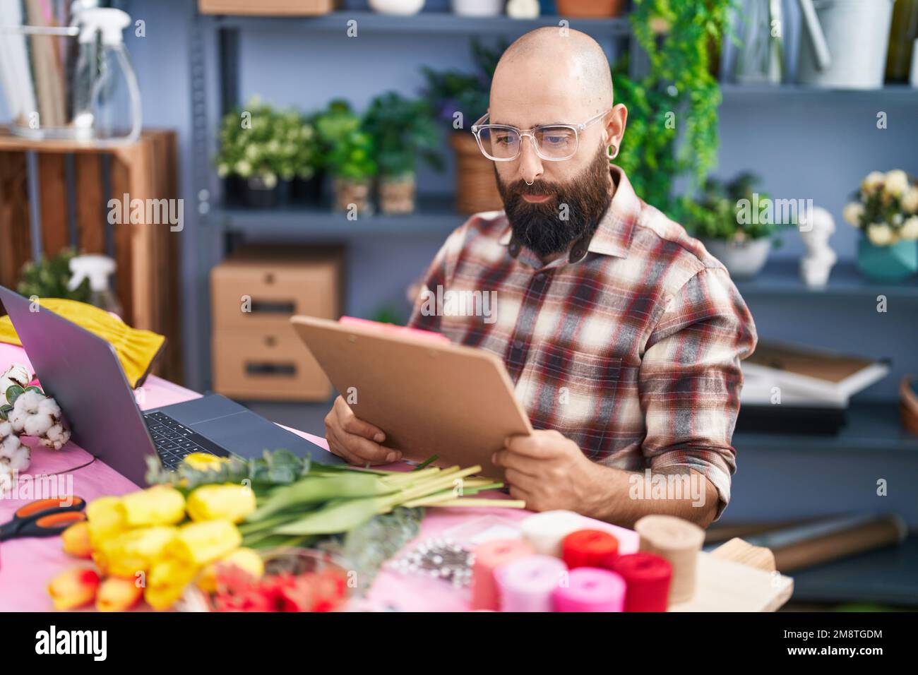 Young bald man florist using laptop reading document at flower shop ...