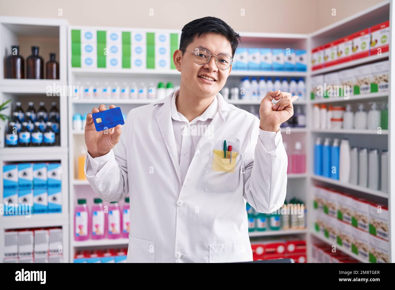 Young asian man working at pharmacy drugstore holding credit card ...